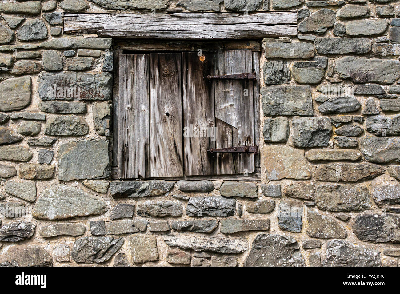 A wooden shutter in a stone wall of irregularly shaped stone Stock ...