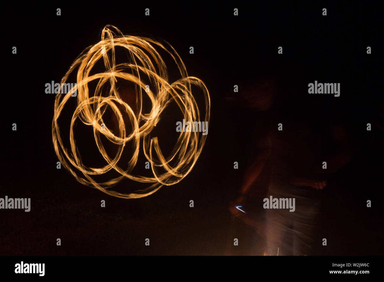 An artist shows a fire show at night spinning torches, circles of fire ...