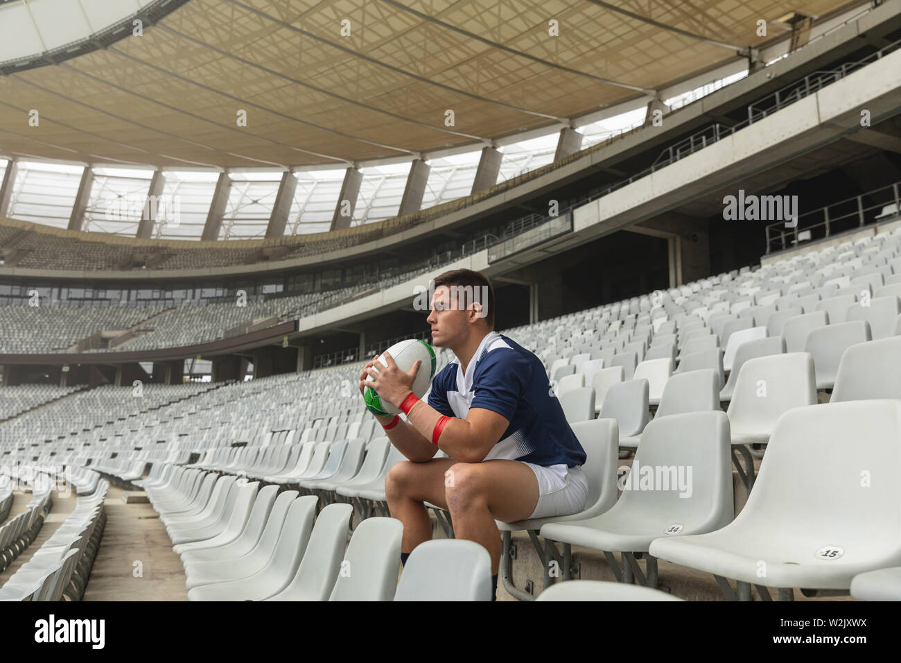 Upset Caucasian male rugby player sitting with rugby ball in stadium ...