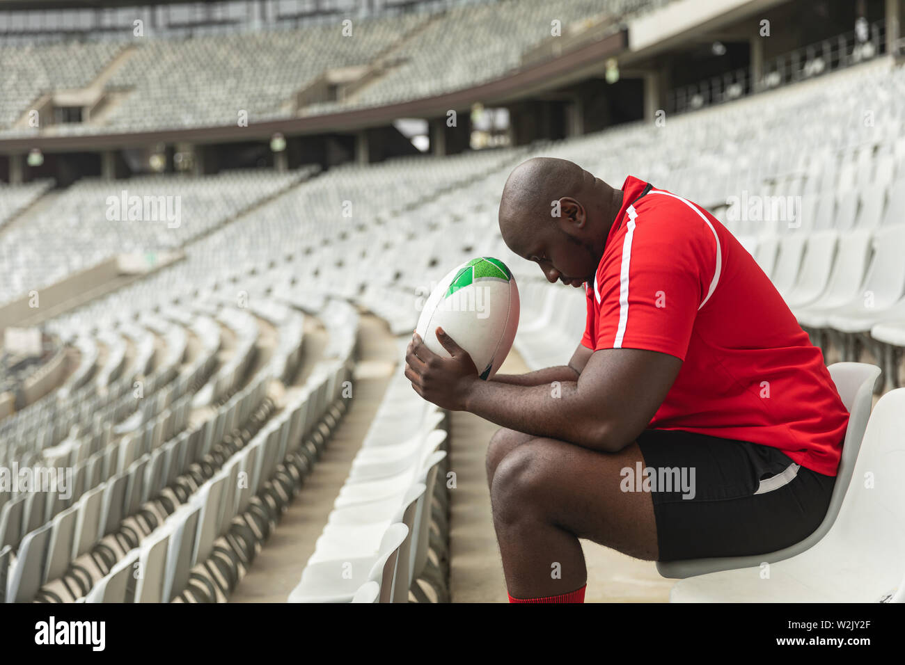 Upset African American male rugby player sitting with rugby ball in ...