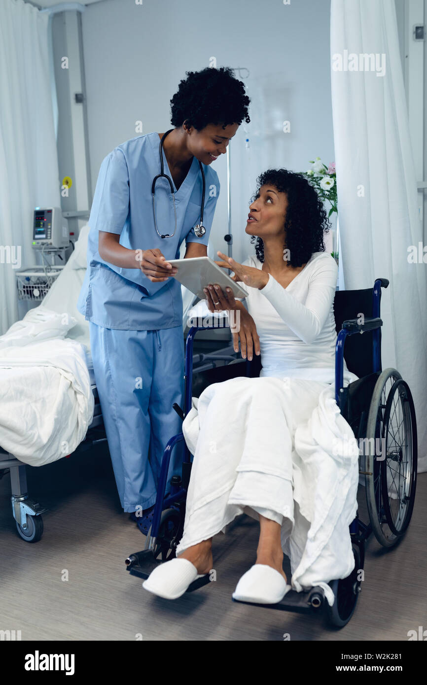 Female doctor helping disabled female patient to use digital tablet in ...