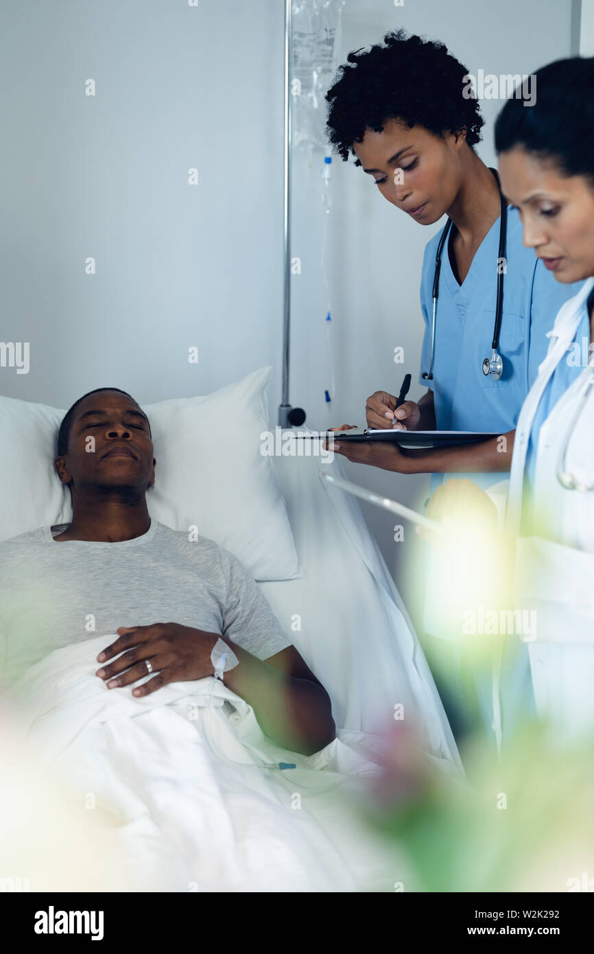 Female doctors checking male patient in the ward Stock Photo - Alamy