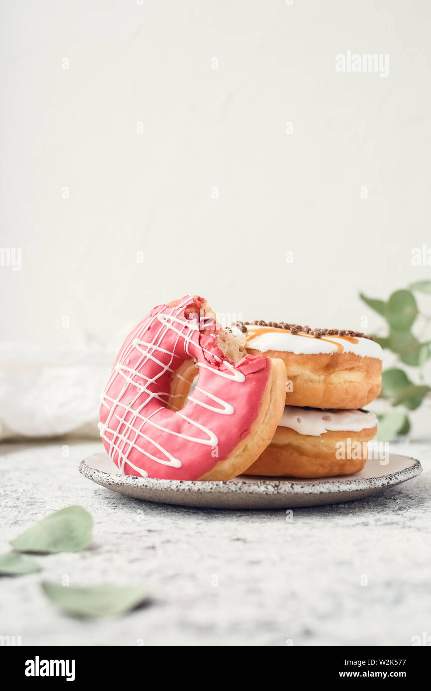 Plate with donuts over light background. Pink frosted donut with bite ...