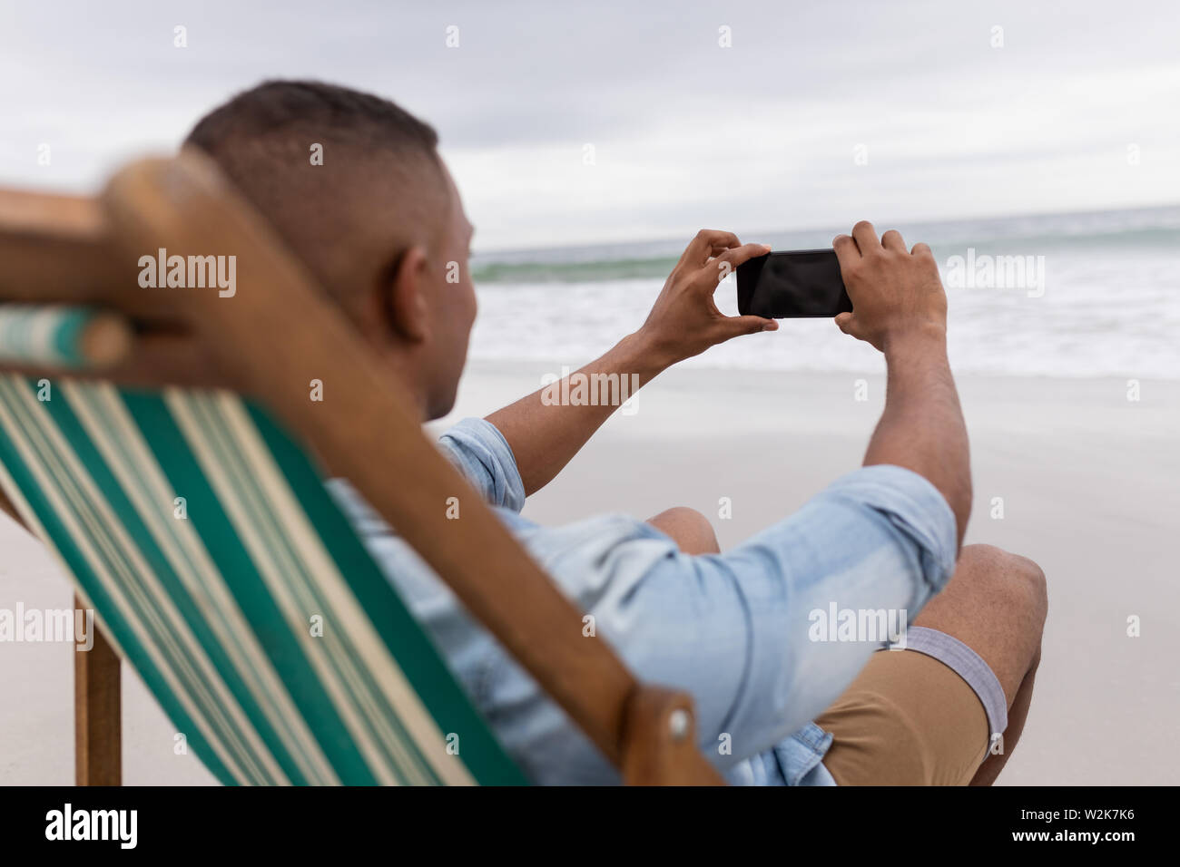 Man clicking pictures with mobile phone while sitting on a beach chair ...
