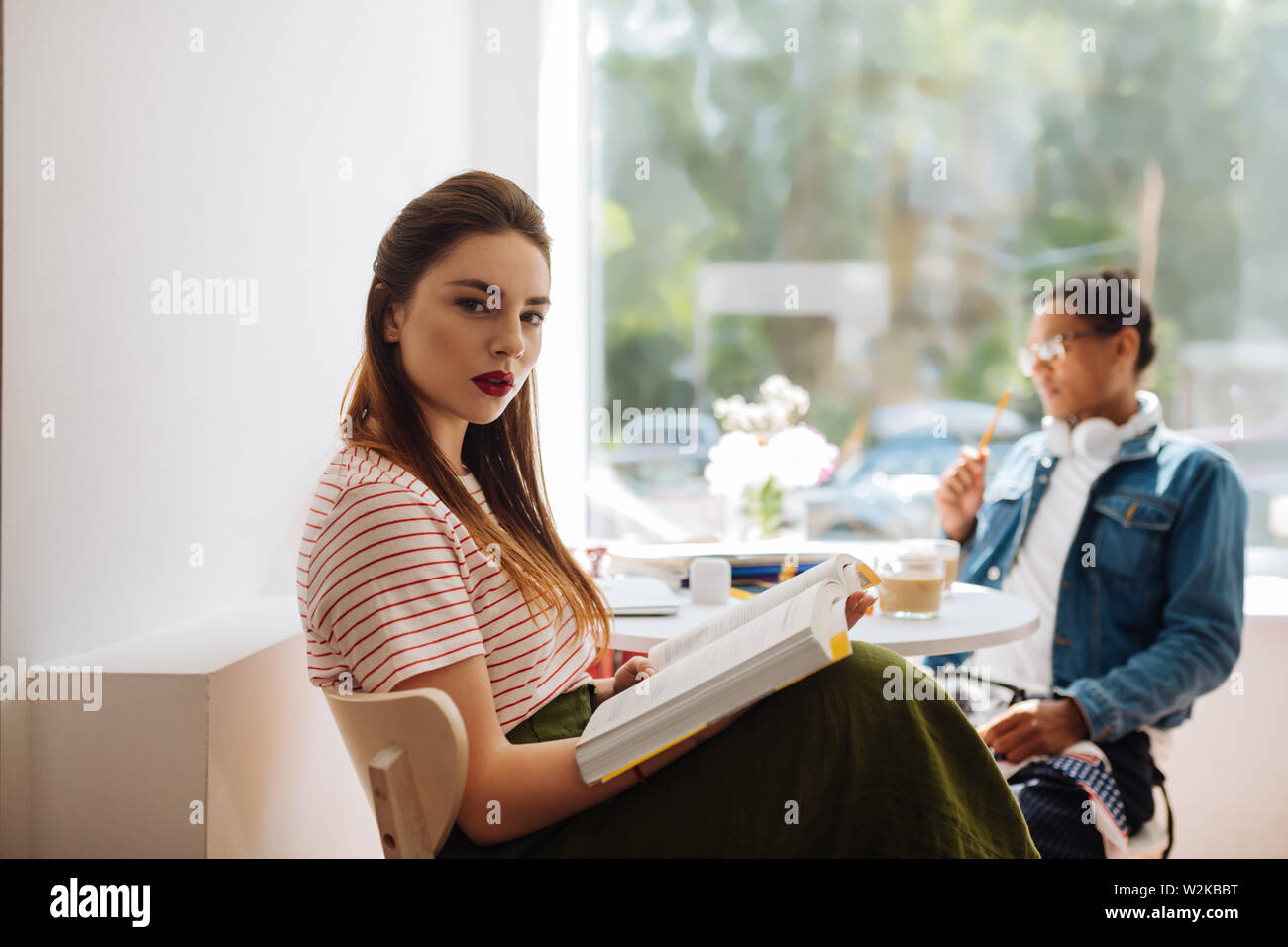 Young beauty. Pretty female with red lips sitting in semi position and ...