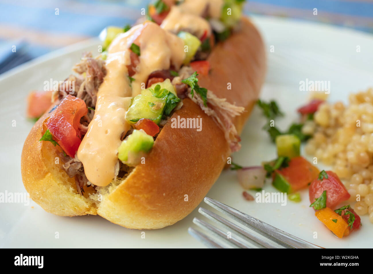 Hot dog and pulled pork on a bun topped with Israeli salad and dressing ...