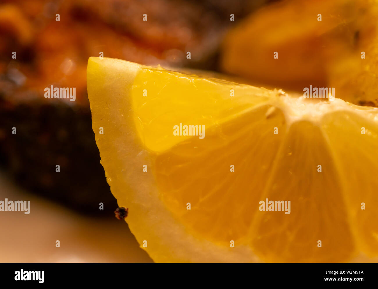 Close-up of a fresh yellow lemon quarter in front of a blurred ...