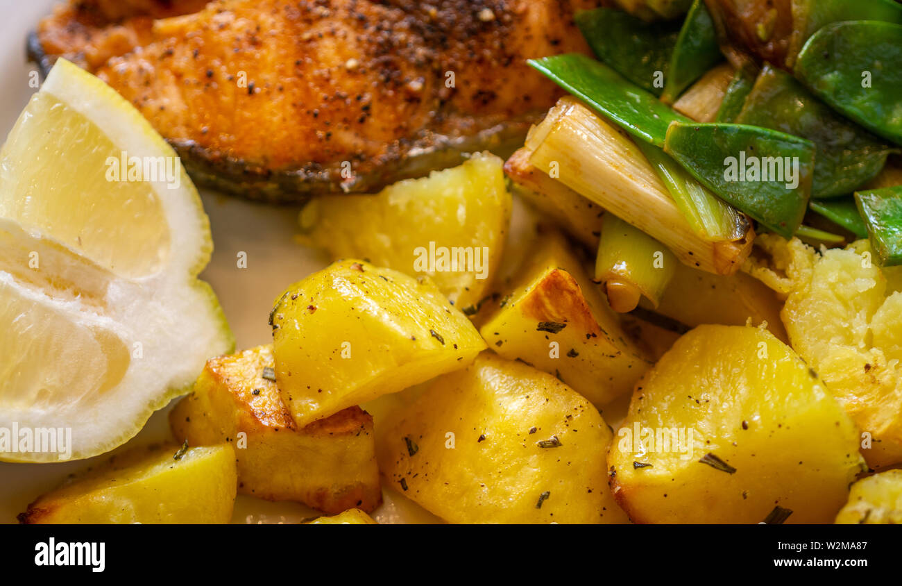 Close-up of salmon cutlet with potatoes on spring onions and sugar snap ...