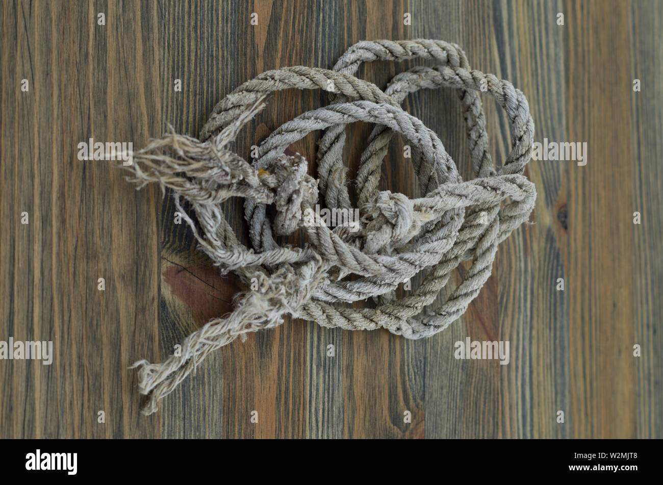 Vintage rope, old rope resting on wooden board. Curled with knots at ...
