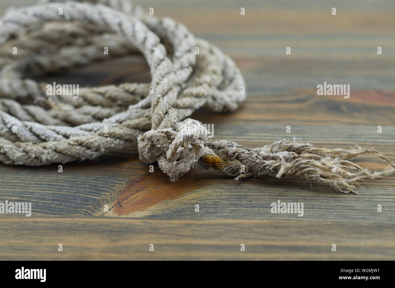 Vintage rope, old rope resting on wooden board. Curled with knots at ...