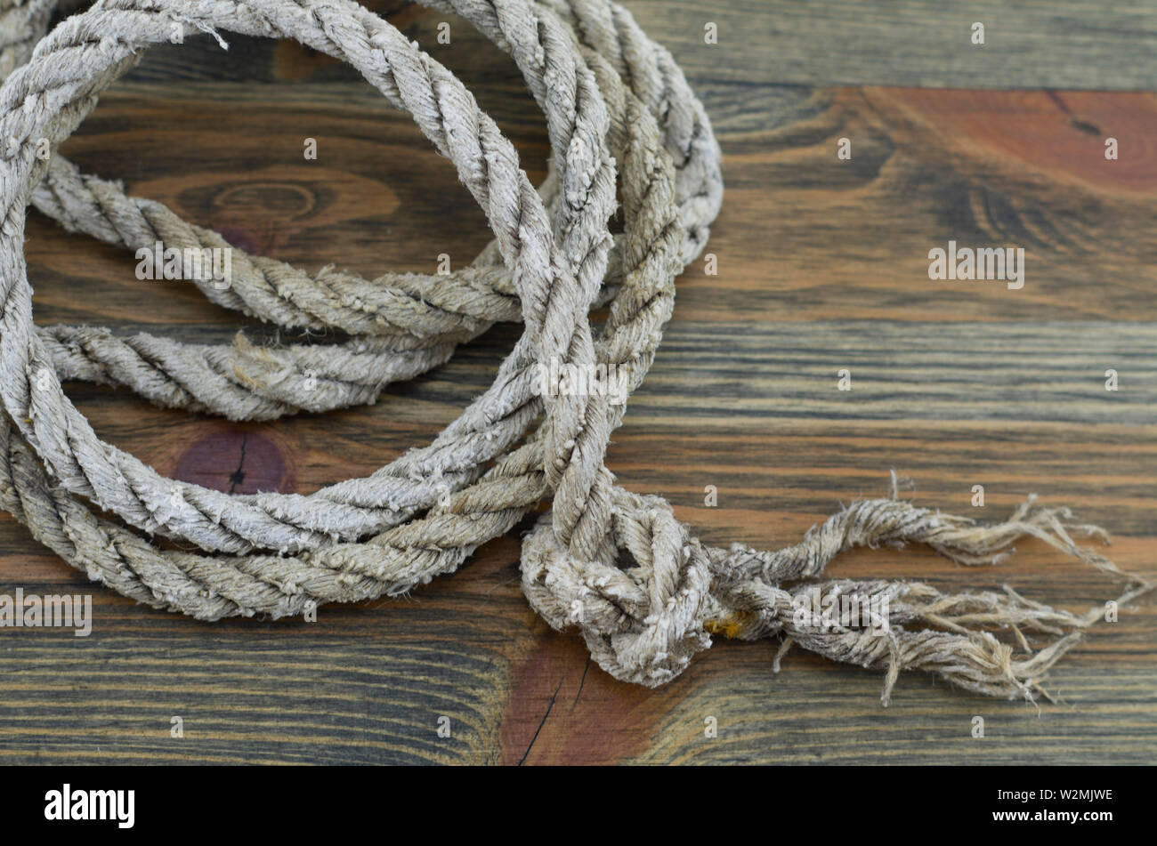 Vintage rope, old rope resting on wooden board. Curled with knots at ...