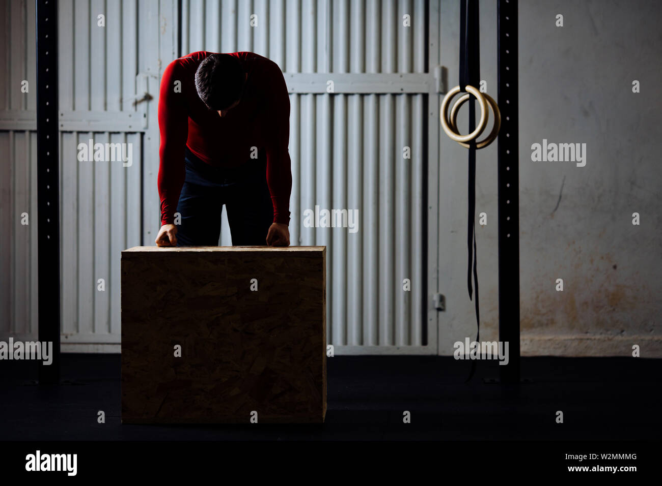 Tired sports man after box jumping exercise leaning on box. Dark ...