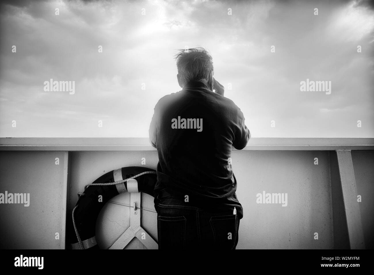 A man from behind on the deck of a ship looking at the sea and talking ...