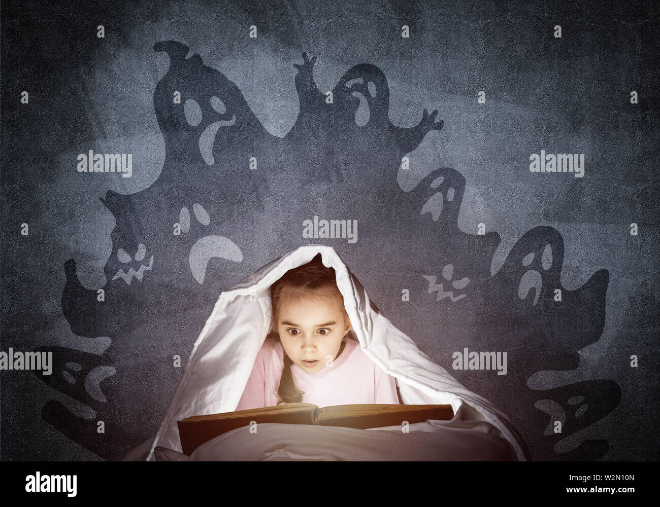 Scared little girl reading book in bed Stock Photo - Alamy
