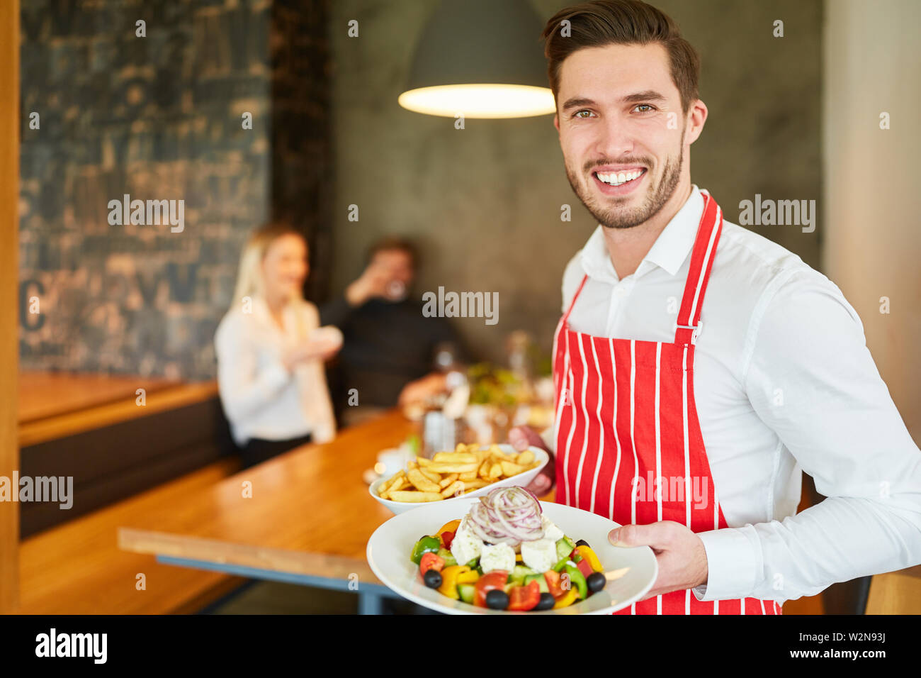 Young man serving as a waiter serving greek salad with feta in the ...