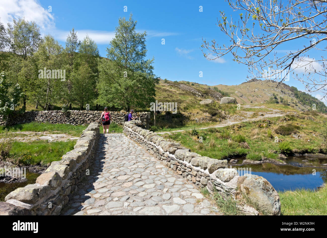 Walkers people walking across stone bridge and footpath Watendlath in ...