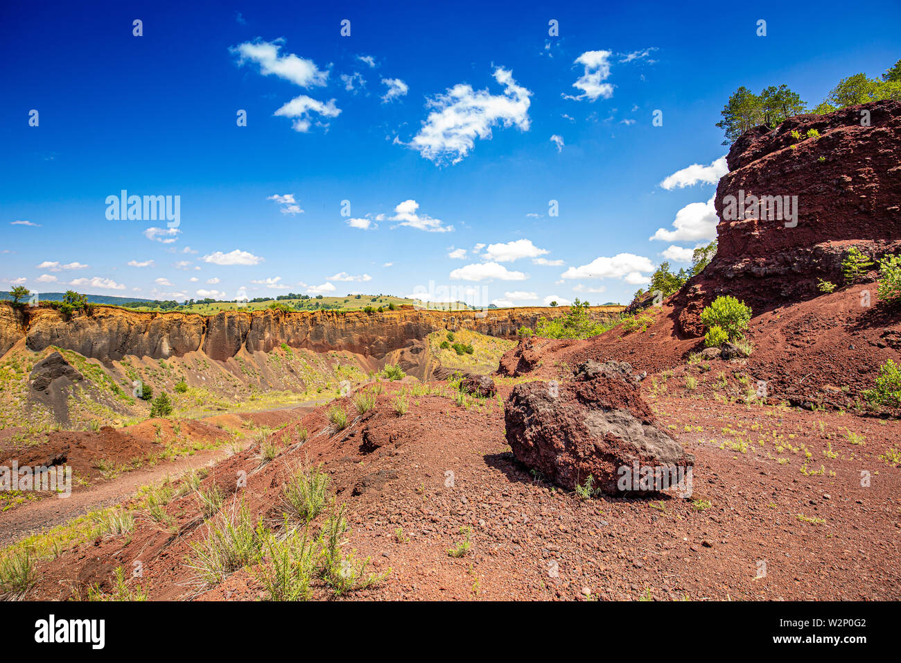 Remains of a volcano, trees in the crater contrasts with the rusty red ...