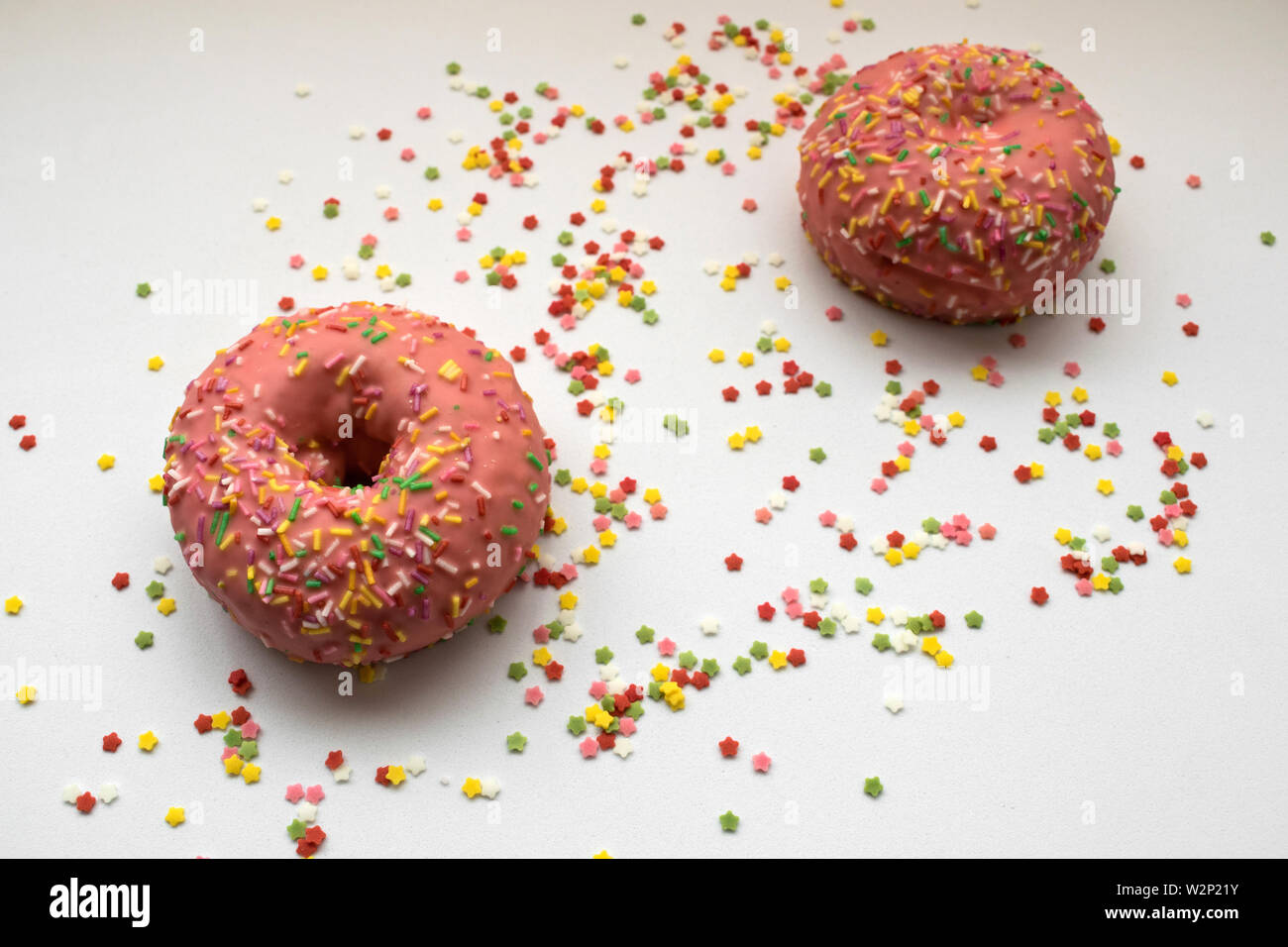 two pink donuts with sprinkles on a white background Stock Photo - Alamy