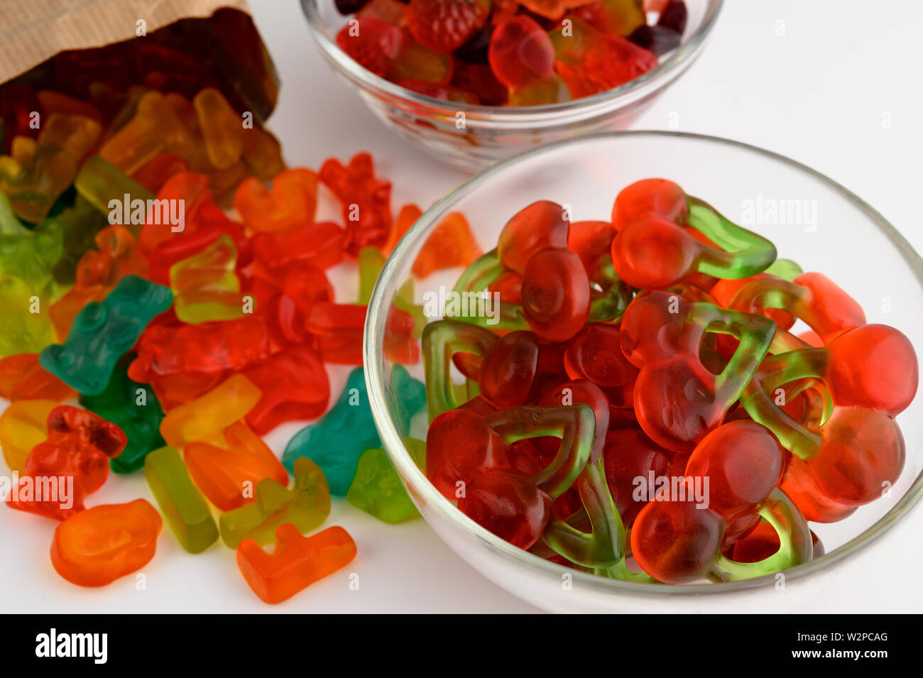 Glass bowls and paper bag of colorful gummy candies on white background ...