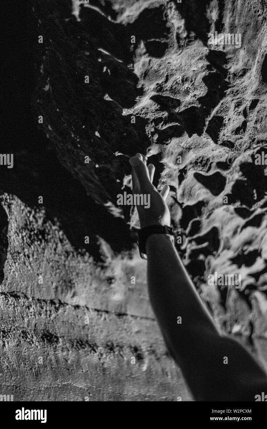 Male's hand reaching and touching the rocks in a cave shot in black and ...