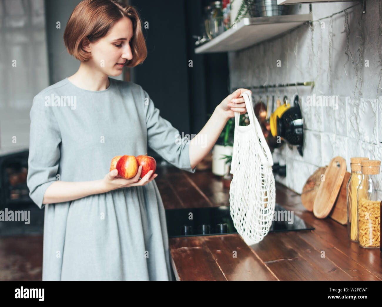 Young woman in the grey dress pulls apples out of knitted rag bag ...