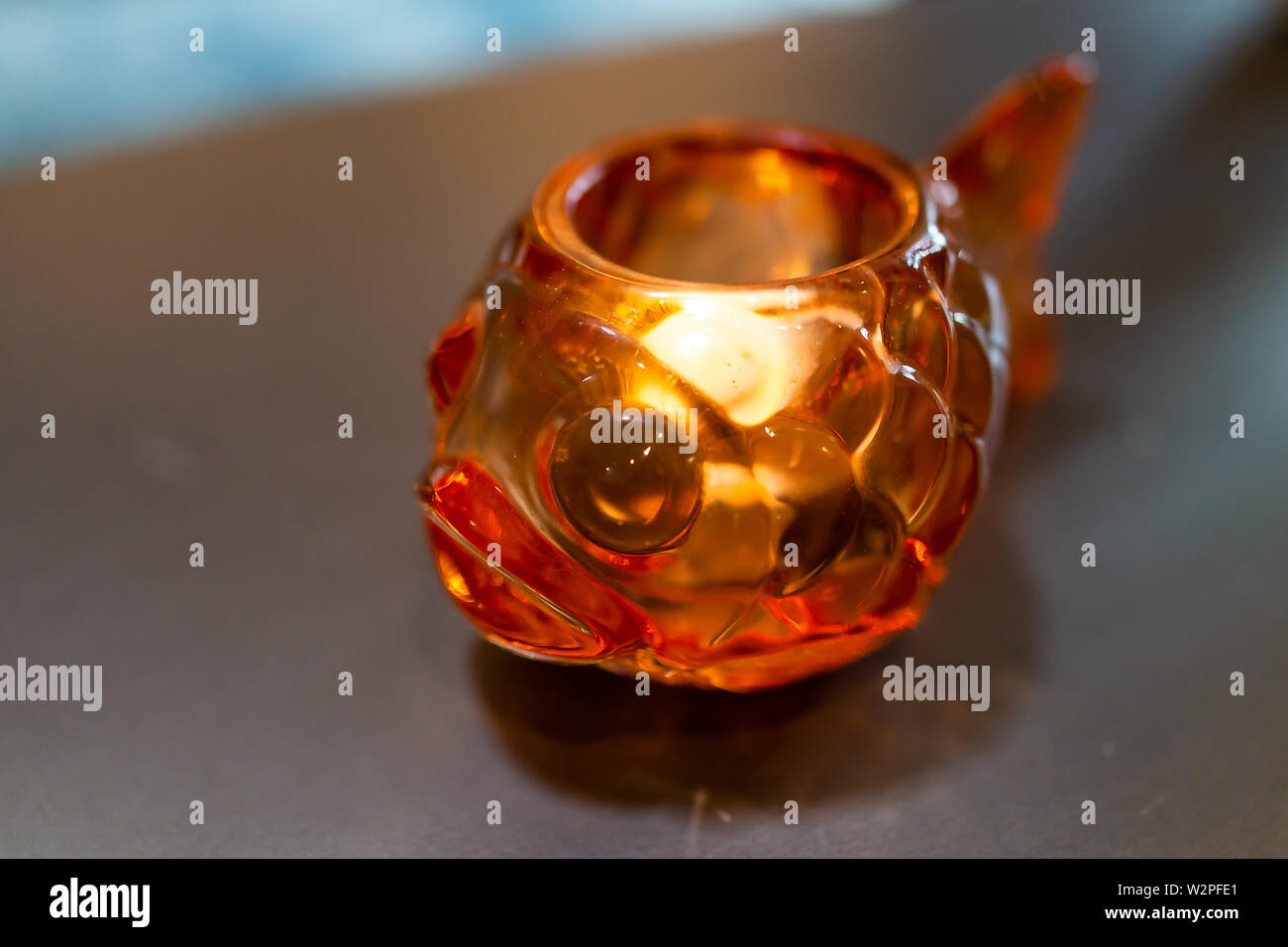 Closeup of glass object with illuminated lit tea candle lamp on table ...