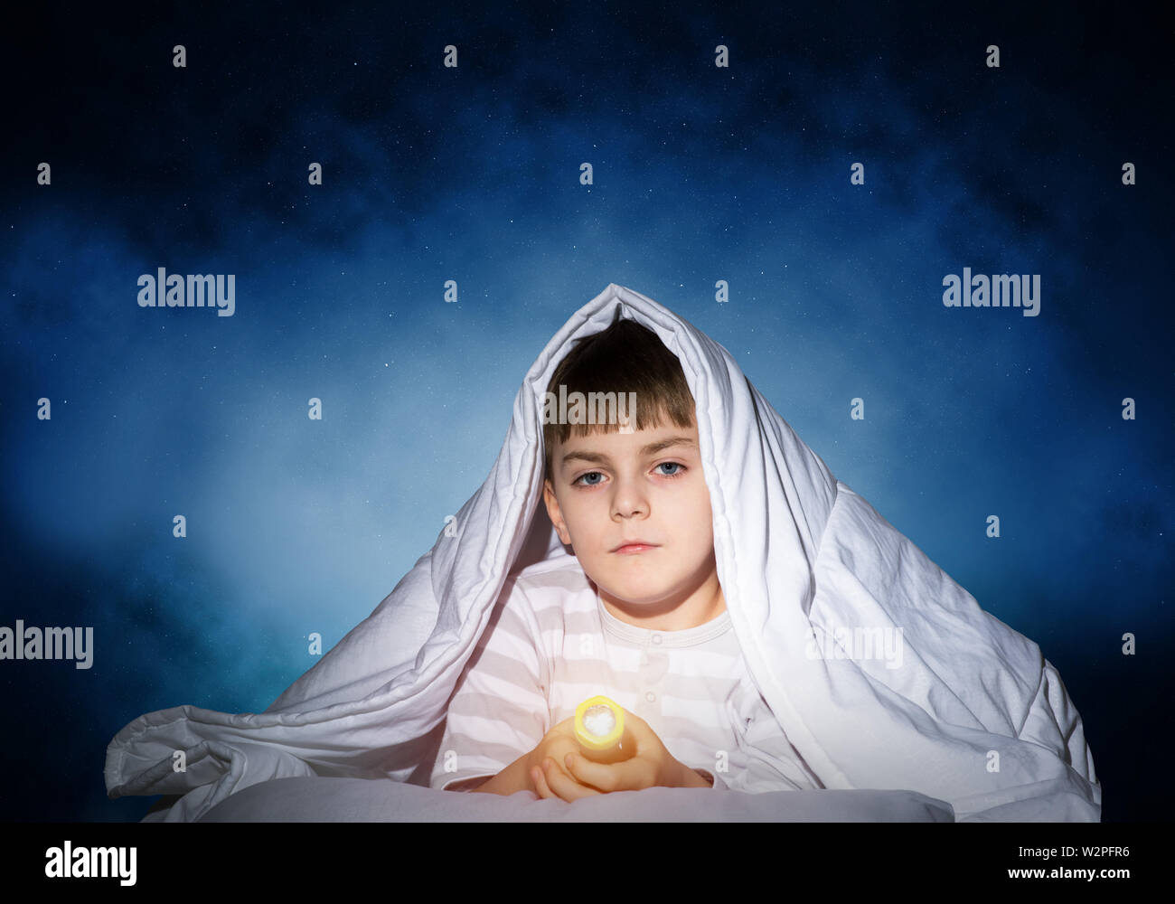 Serious child with flashlight hiding under blanket Stock Photo - Alamy