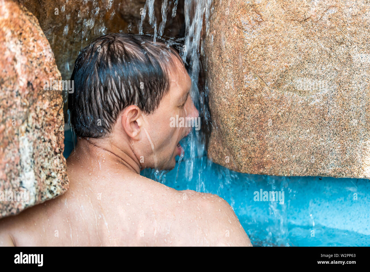 Young man swimming under waterfall in Japanese spa by stone pool ...