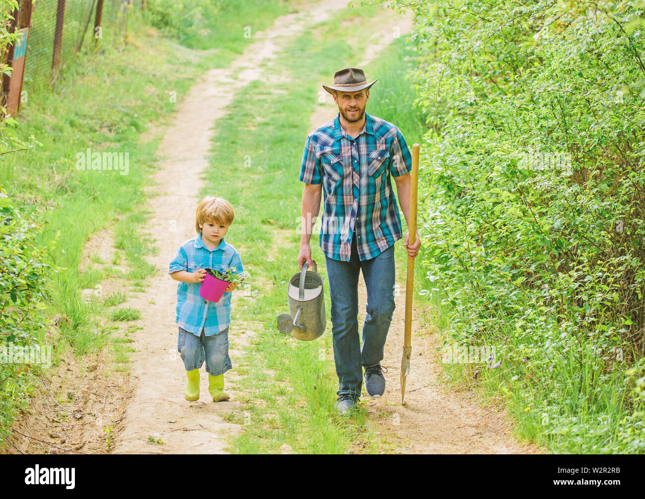 Boy and father in nature with watering can and shovel. Dad teaching son ...