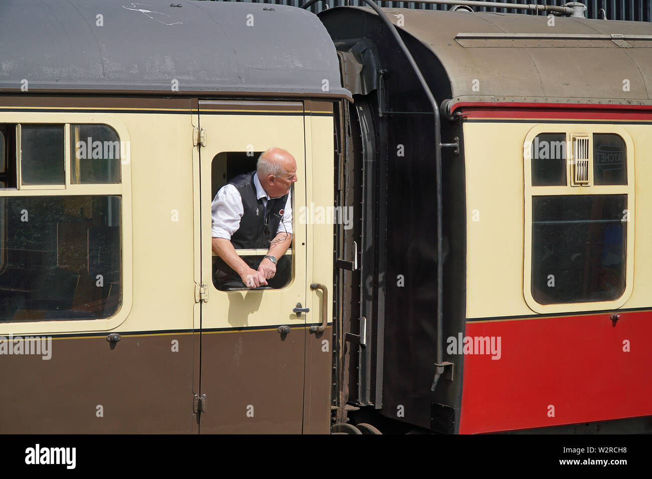 A railway guard looks anxiously out of a carriage window while waiting ...