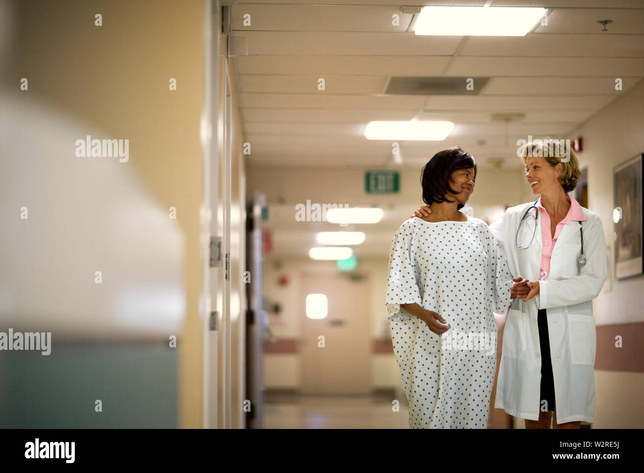 Doctor helping her patient to walk down the corridor for the first time ...