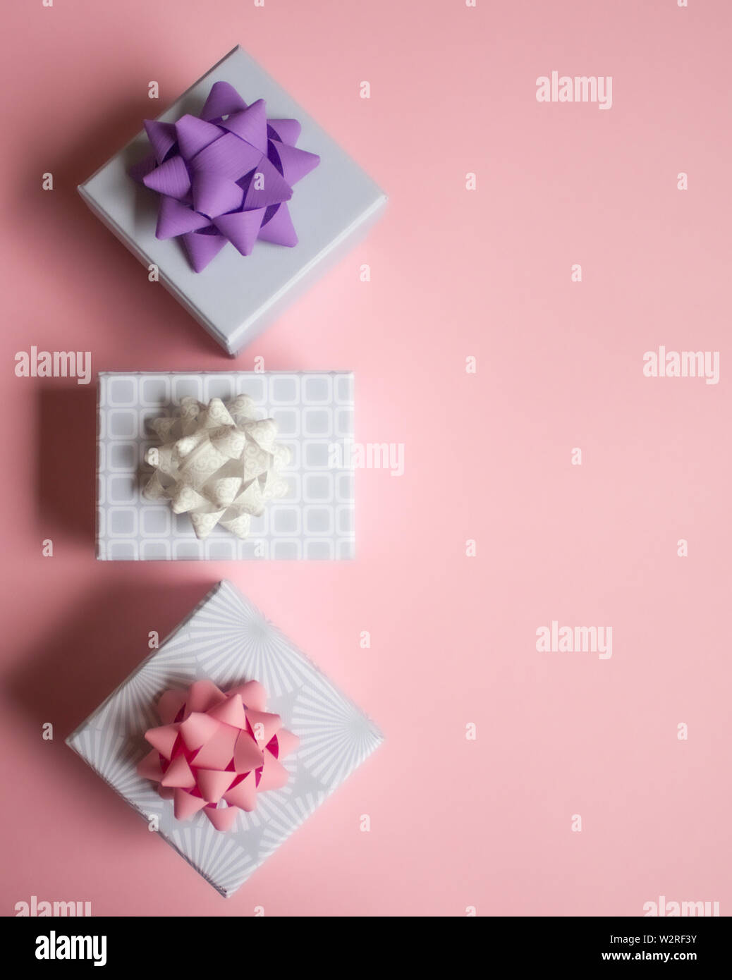 Three light gray gift boxes with colorful bows on pink background ...