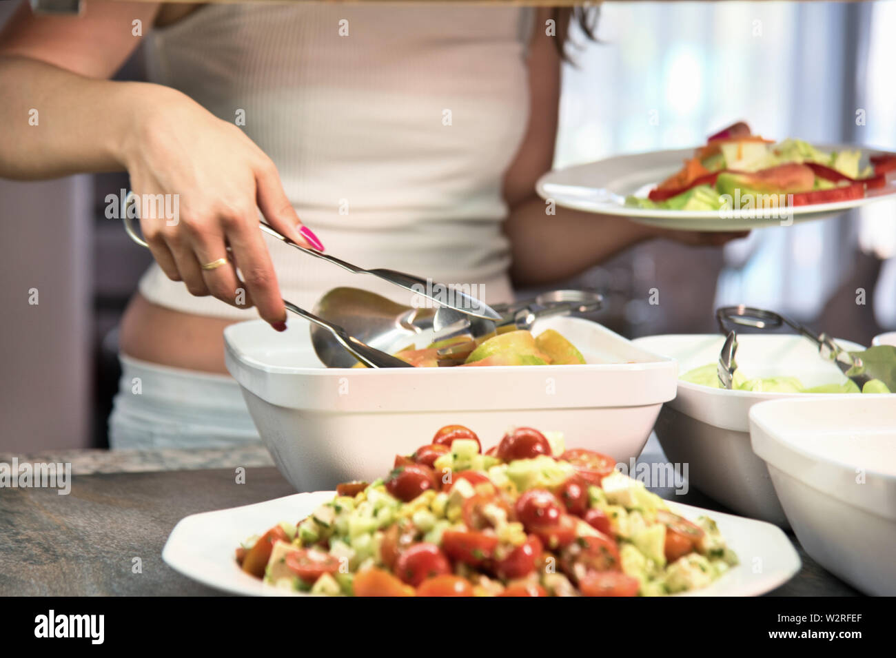 Close-up of hands of a young woman serving cooked food and vegetables ...