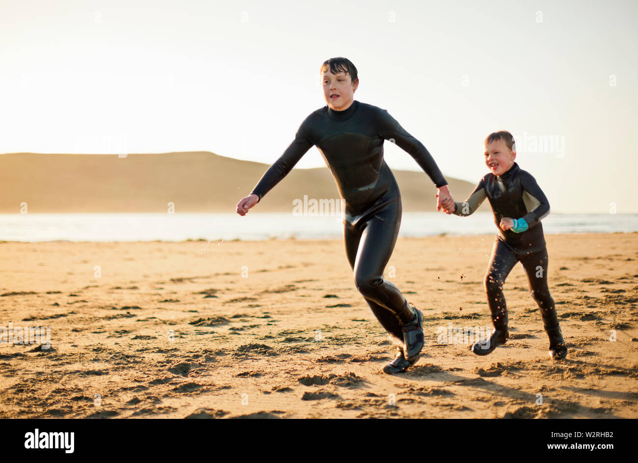 Young brothers running along the beach in wetsuits Stock Photo - Alamy
