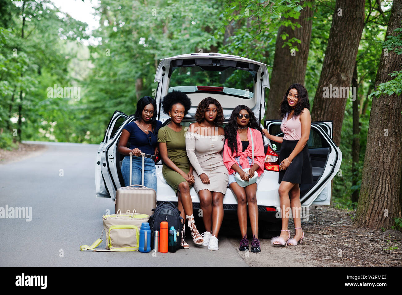 Group of five happy african american traveler girls sitting in car open ...