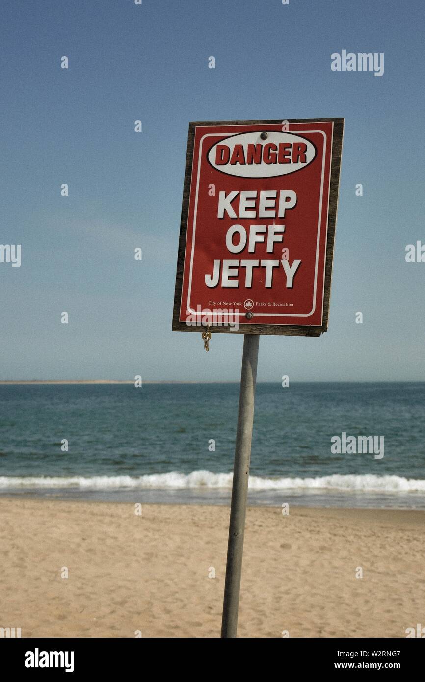 Red sign at the sandy beach that reads "DANGER KEEP OFF JETTY" with the ...