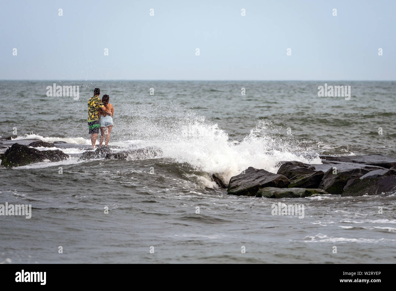 A romantic couple of young people on a stone mole on the ocean coast ...