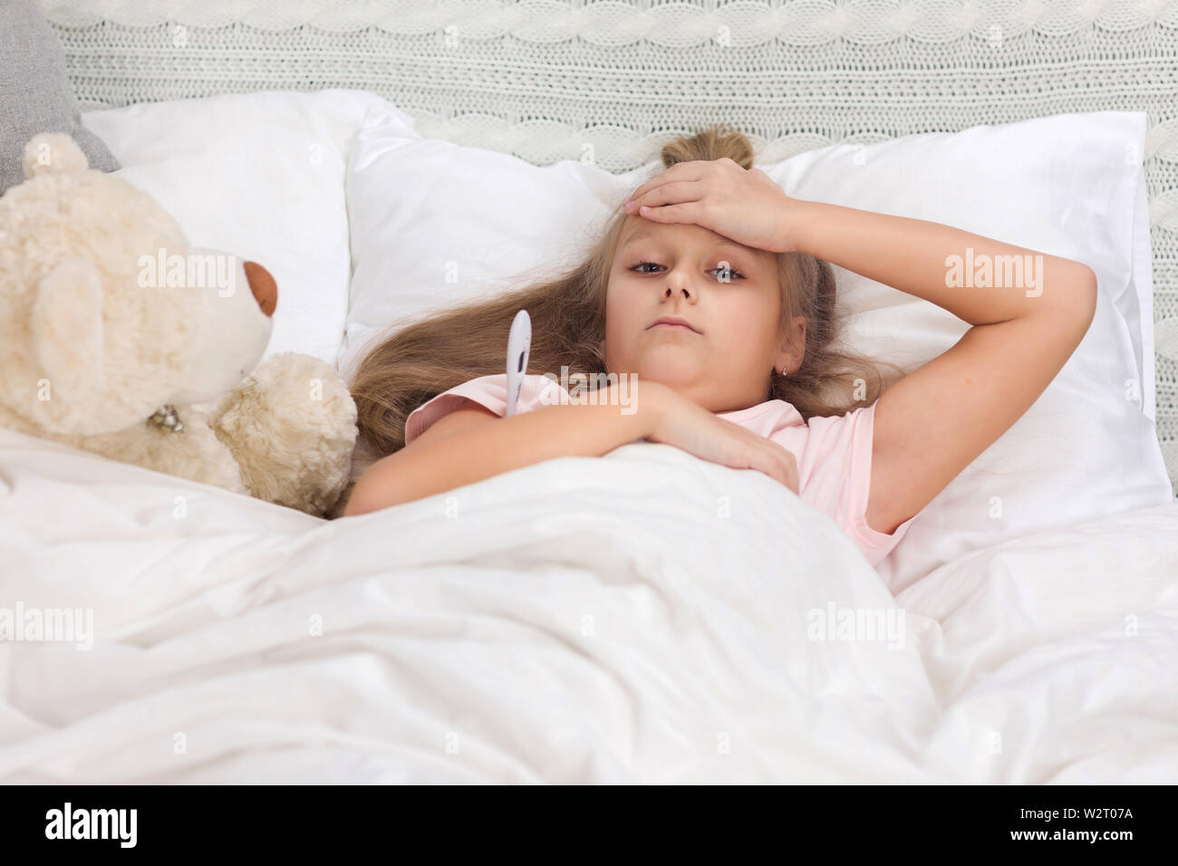 Sick little child girl lying in bed with thermometer. Cold flu season ...