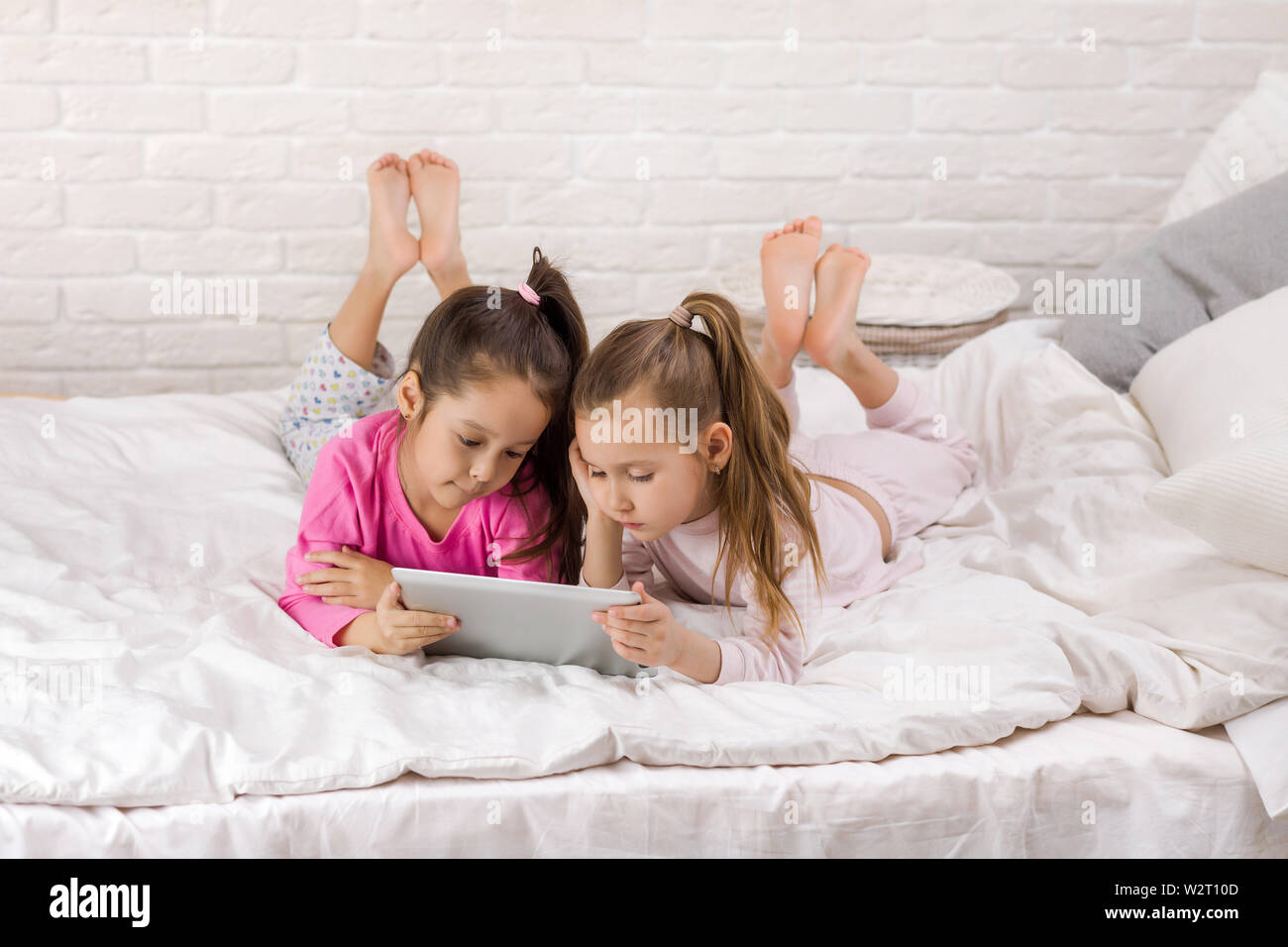 two cute children girls use digital tablet in bed. child playing on ...