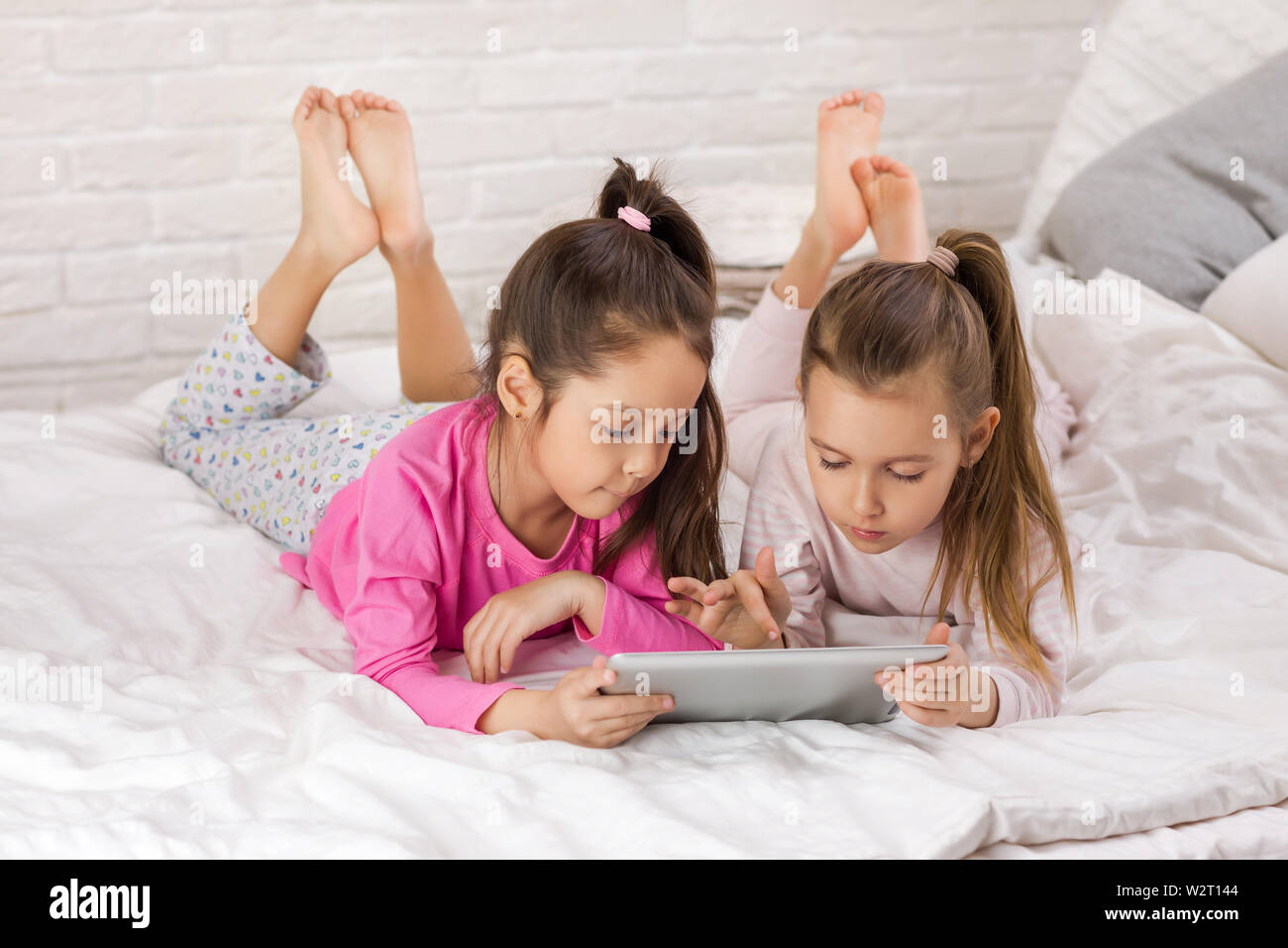 two cute children girls use digital tablet in bed. child playing on ...