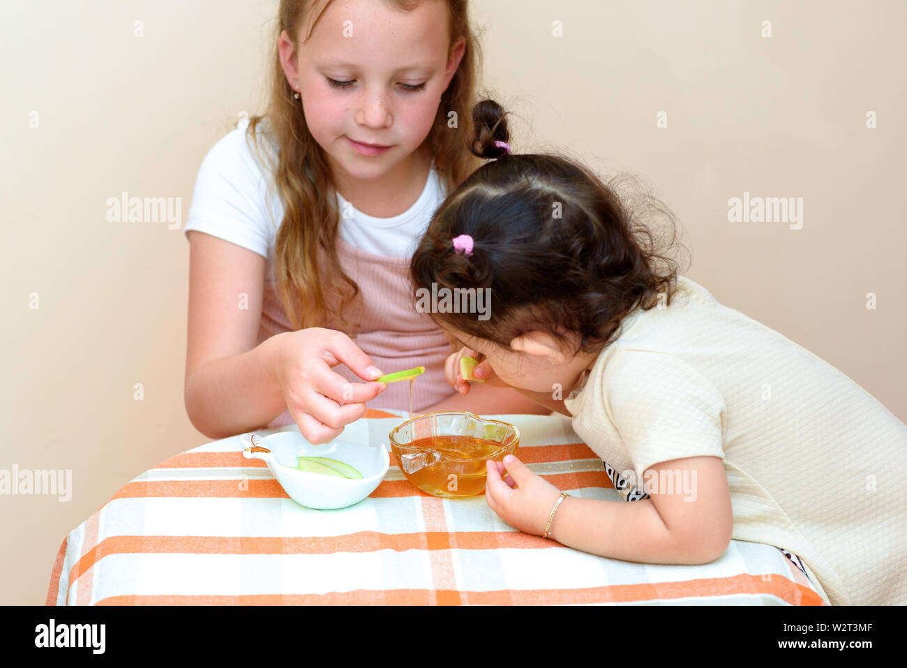 Close up portrait of two funny cute little girl eat apple with honey ...