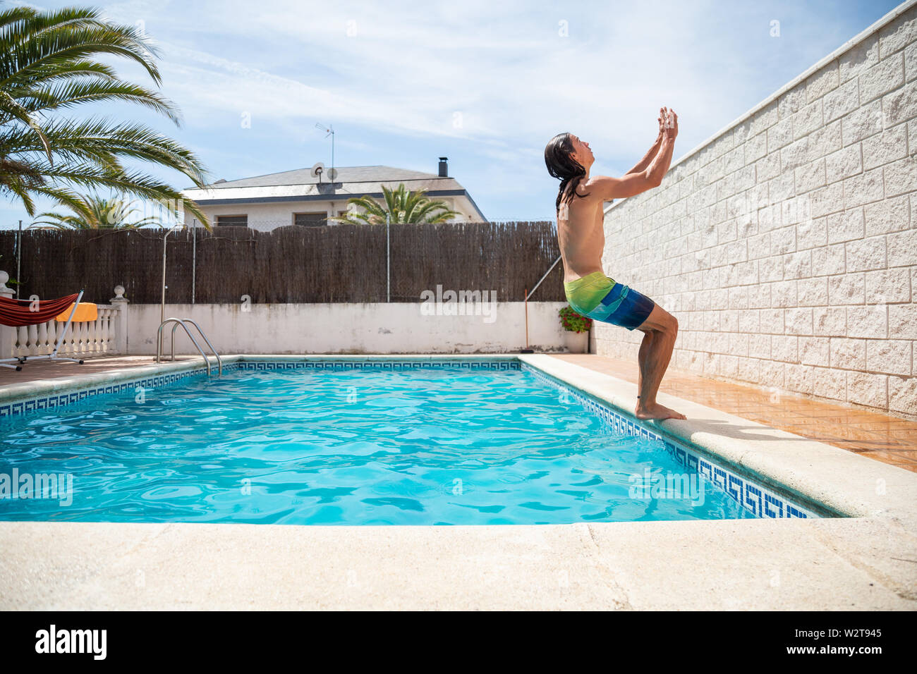 Young fitness man jumping into the water in the pool one day of summer ...