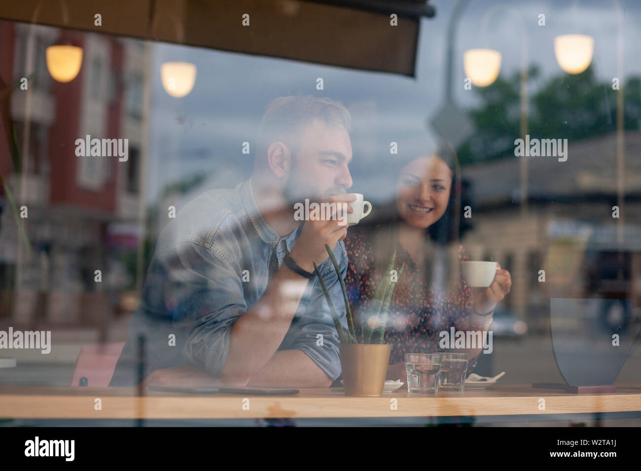 two friends drinking coffee in a cafe. Shot thought window with ...