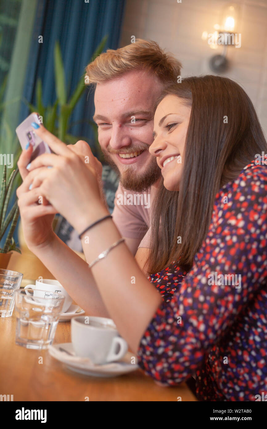 two friends sitting together, smiling while looking at a phone screen ...