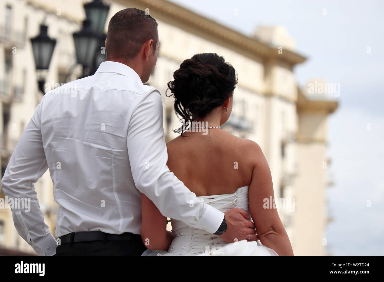 Wedding in a city, groom embraces the waist of bride, rear view. Just ...