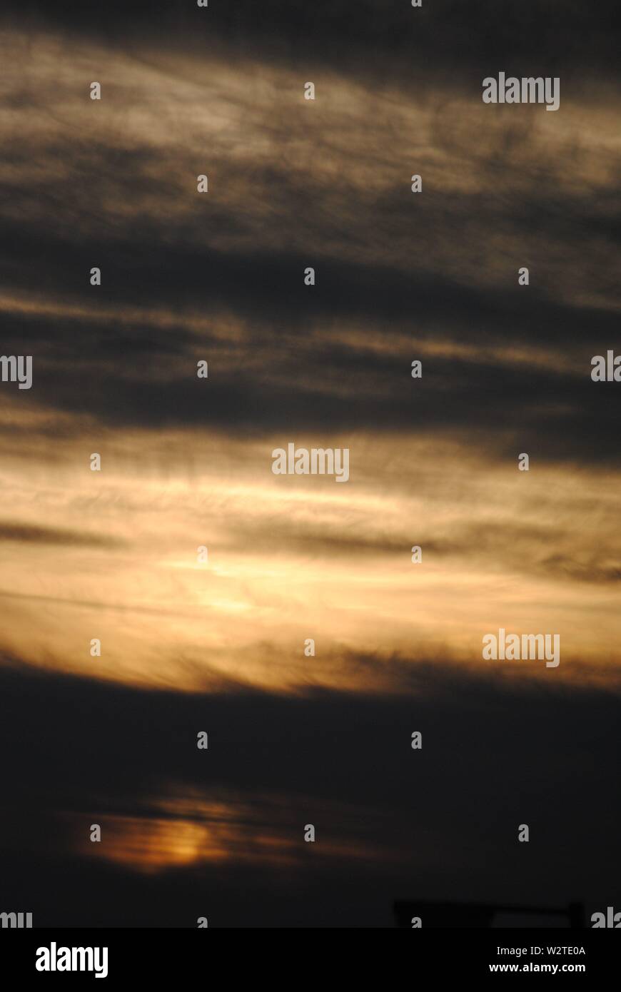 golden glow of the evening sun partly hidden by clouds as it sets in ...