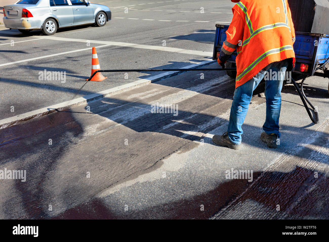 Service road maintenance worker sprays the bituminous mixture onto the ...