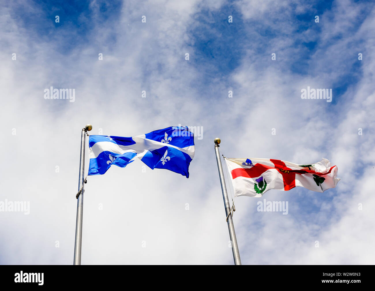 Flags of Quebec and Montreal flapping in wind against sky with clouds ...