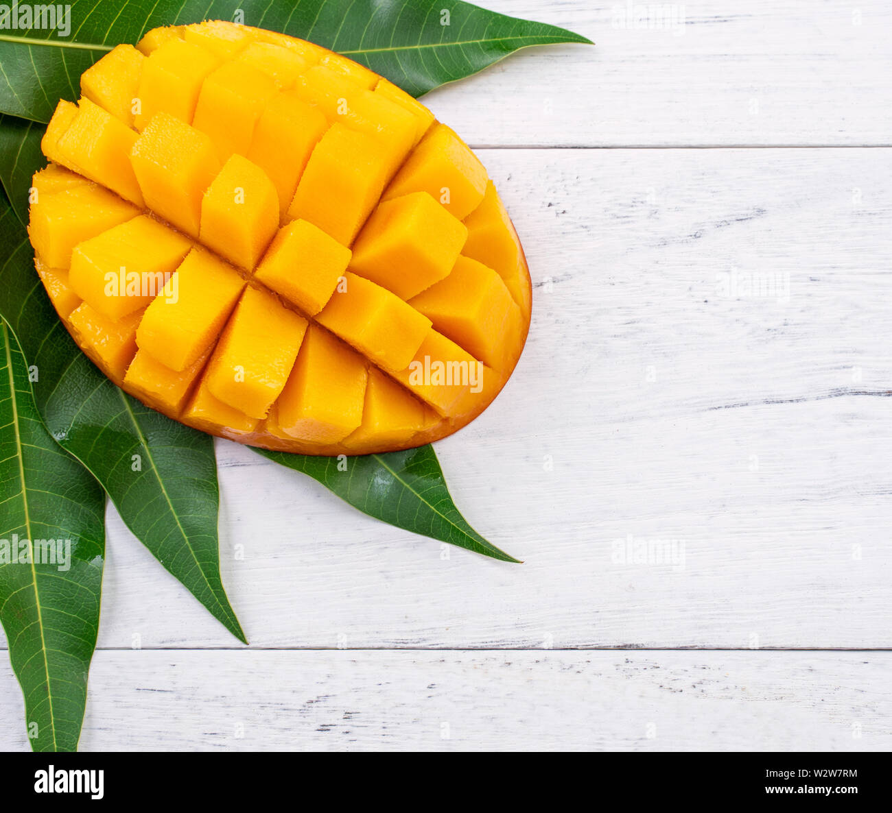 Beautiful chopped mango with green leaves on bright white color timber ...