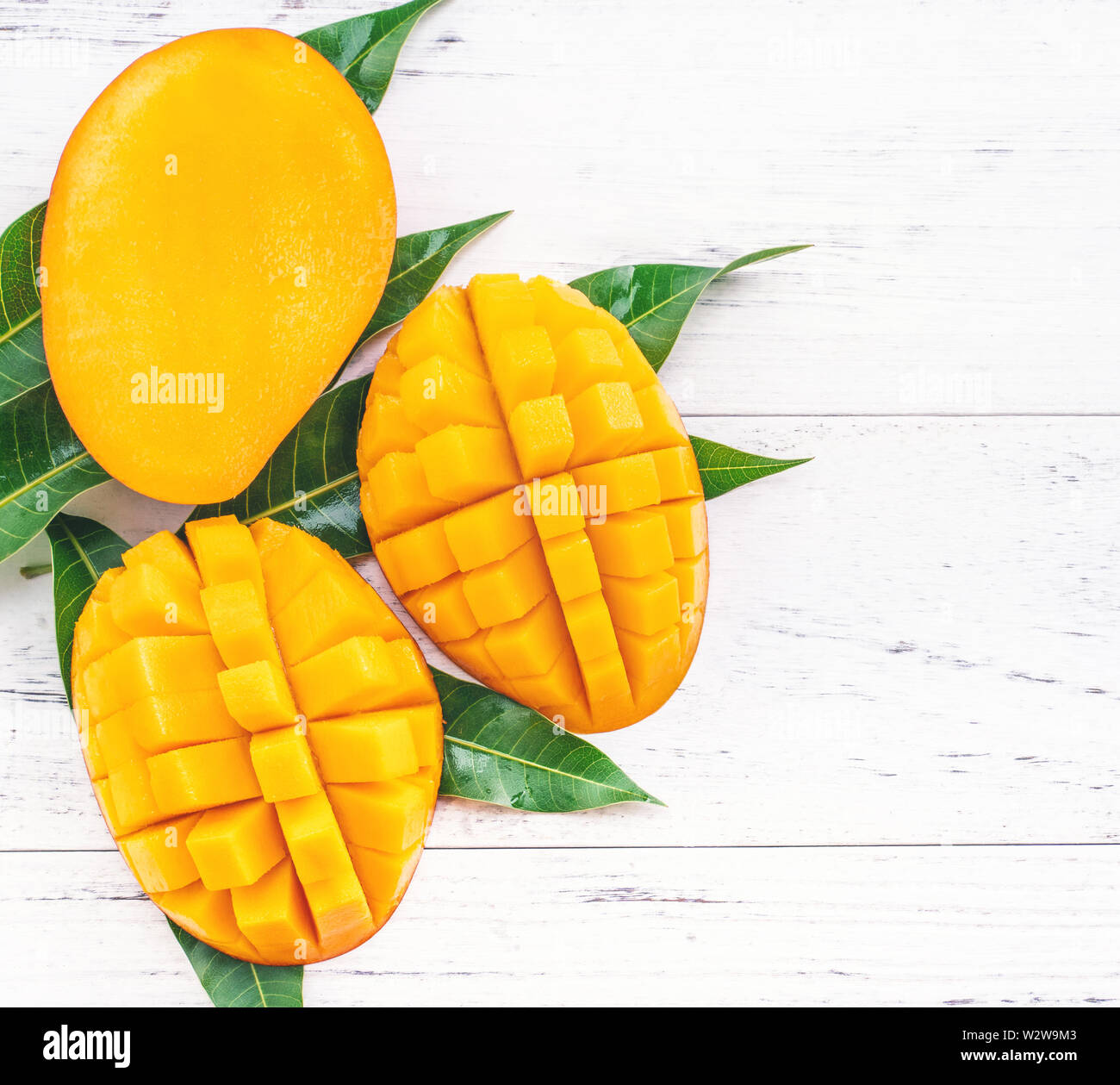 Beautiful chopped mango with green leaves on bright white color timber ...
